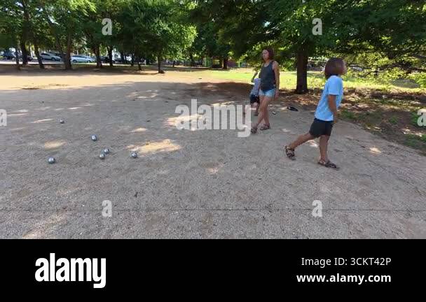 Family playing petanque together in the park. Adults and children take ...