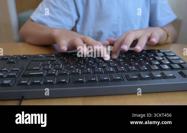 Close-up of child typing on computer keyboard at wooden desk. Concept ...