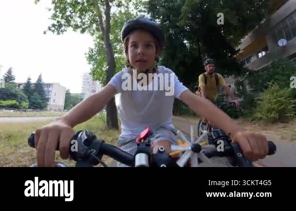 POV of child riding bicycle with helmet on urban path, man following ...