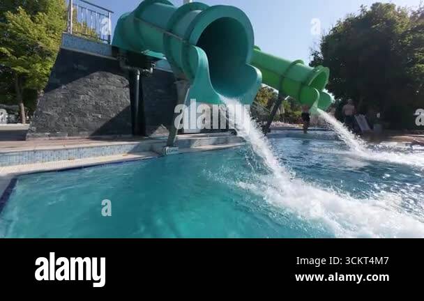 Excited child splashing into the pool from a green water slide at a ...