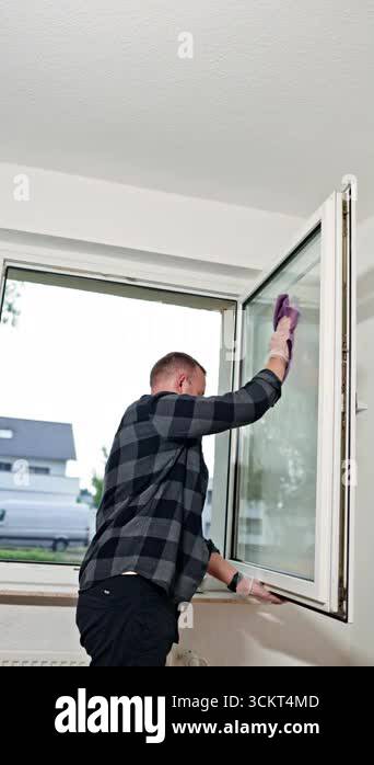 Young man washes windows in house. Professional cleaner rubs windows to ...