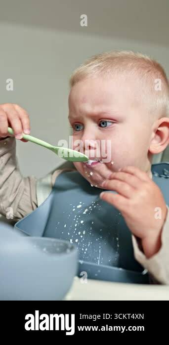 Toddler boy with a spoon in his hand eats milk porridge on his own ...