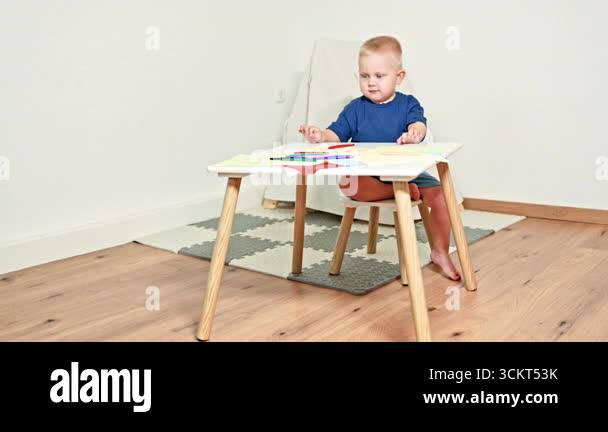 A toddler sits at home at a table and draws with colored pencils on ...