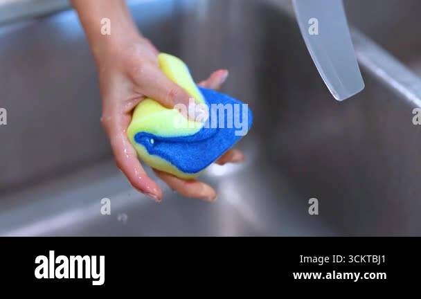 A person cleans a knife with a sponge in a kitchen sink, highlighting ...