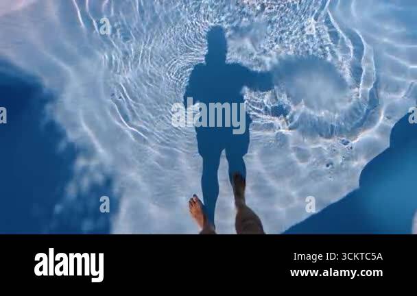 Man standing in clear pool water with visible shadow and sunlight ...