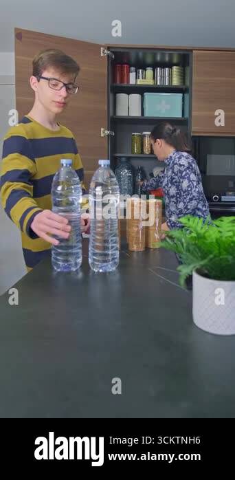 Teenage son and mother storing water bottles and cookies packaged, food ...
