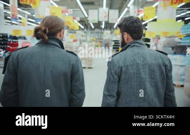 Two serious man walking in supermarket frame behind shopping customer ...