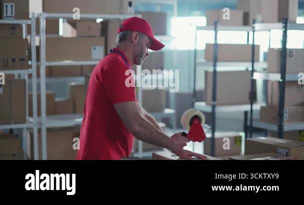 Post office. Caucasian worker in red uniform and cap packing carton ...