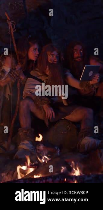 Cavemen gather around a campfire, amazed by a modern tablet, blending ...