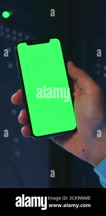 A hand is holding up a smartphone that features a bright green screen ...