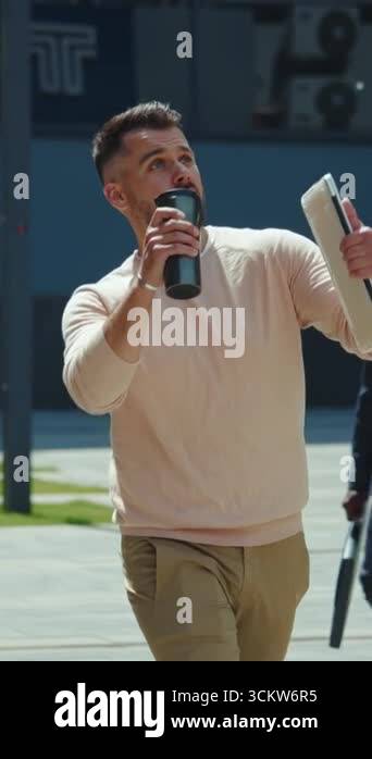 A young man in a beige sweater runs with a laptop outdoors, showcasing ...