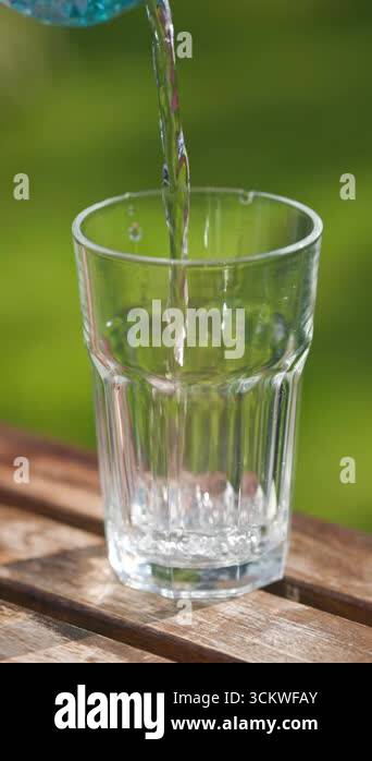 fresh cold water pouring into glass from bottle on wooden table on ...