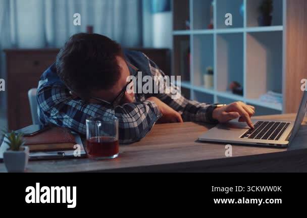 A tired person rests on a cluttered desk, surrounded by work, showing ...