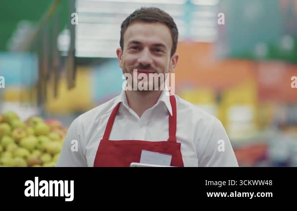 Close up face seller man in supermarket look camera smile vegetable ...