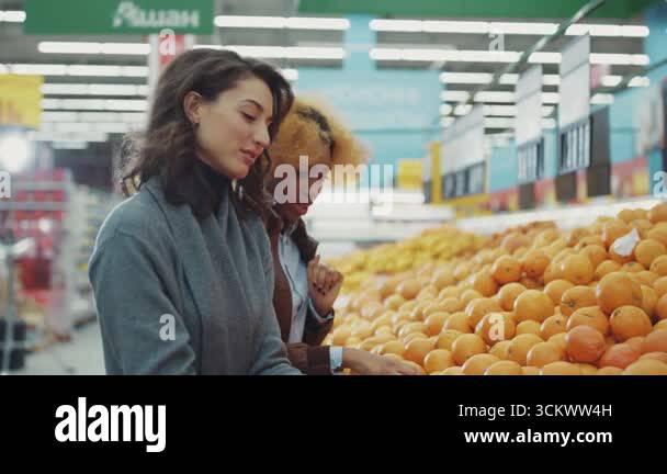Two cute young women chooses orange in supermarket walk smile food ...