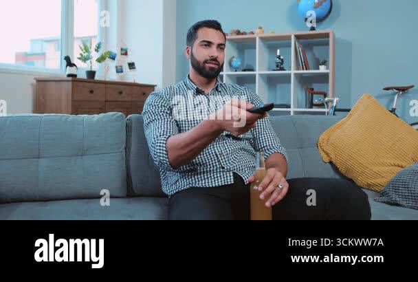 Portrait of a young smiling attractive man drinking beer watching tv ...