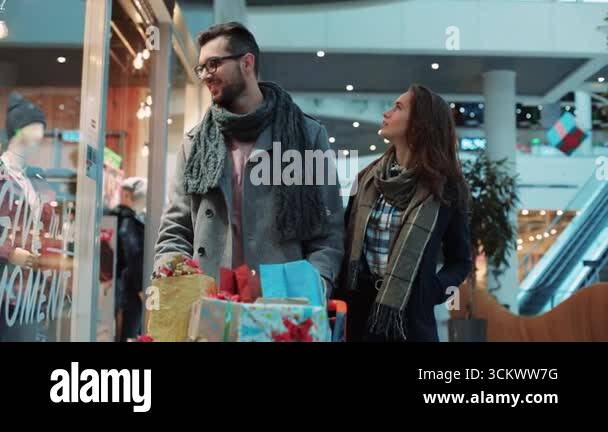 Portrait young couple with Christmas present walk in a mall smiling ...