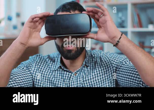 Young attractive man uses virtual reality glasses sitting at sofa ...