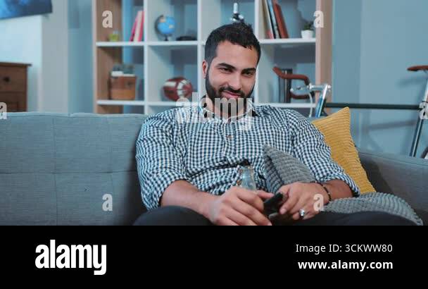 Portrait of a young smiling attractive man drinking beer watching tv ...