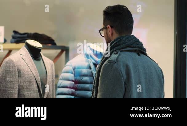 Young attractive man looking at shop window with mens suits in the mall ...
