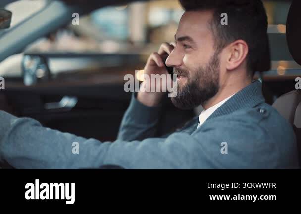 Good-looking guy with beard sitting on drivers seat of car and talking ...