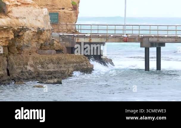Dynamic ocean waves crash against rocky cliffs and a bridge in Port ...