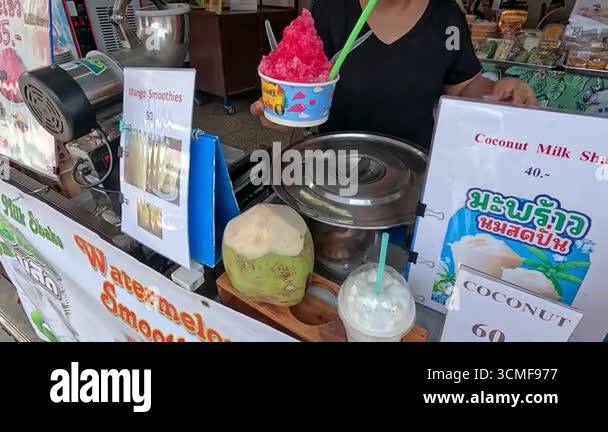 A vendor prepares and serves vibrant shaved ice at a bustling street ...