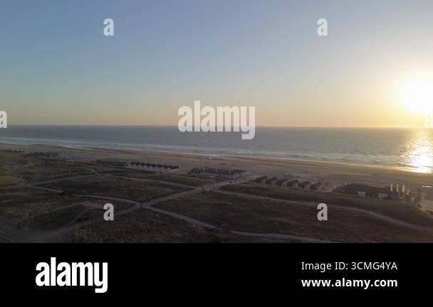 A golden sunset over the calm sea and sandy beach, with dunes, pathways ...