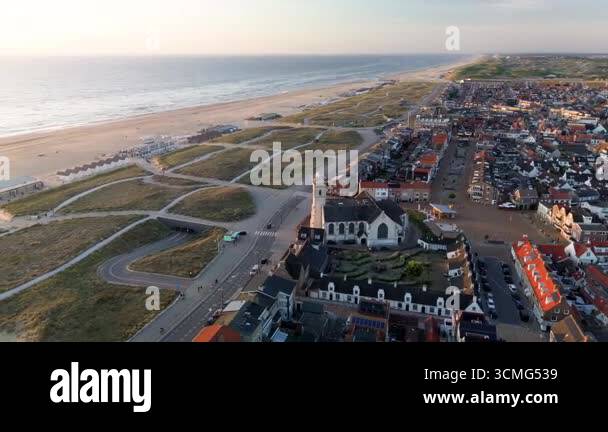 Aerial view of a seaside town at sunset, showing red-roofed houses, a ...