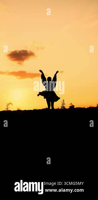 Silhouette of a young happy girl in a dress spinning around herself ...