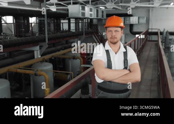 Portrait of a young worker in a uniform and a hard hat looking at the ...