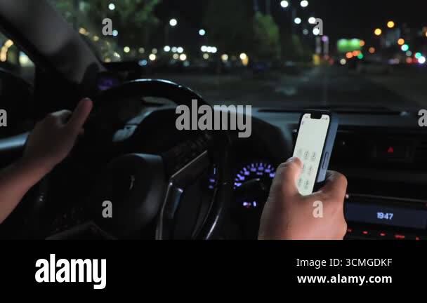 Close-up of man holding smartphone while driving a car at night on city ...