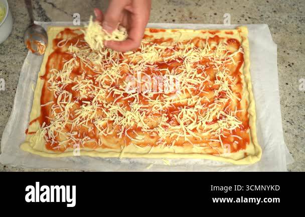 A man makes homemade pizza by adding grated mozzarella cheese to tomato ...