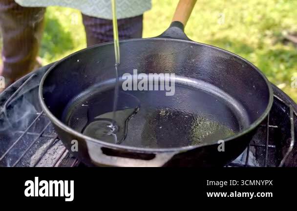 Close-up of a cook pouring olive oil into a hot cast iron pan that is ...