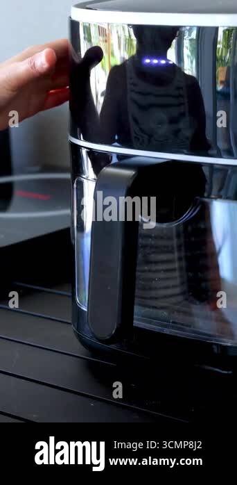 Hands operate an air fryer, removing cooked food in a bright kitchen ...