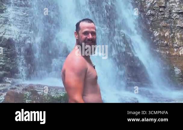 A young attractive traveler stands under the stream of a mountain ...