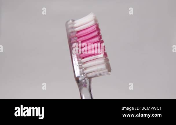 A detailed view of a pink and white toothbrush with a clear handle on a ...