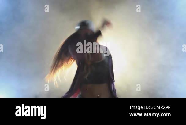 Dancer emerging from backlit fog, spinning, raising arms responding to ...