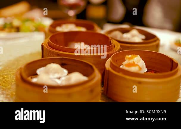 Hands selecting dim sum from bamboo steamers in a warmly lit restaurant ...
