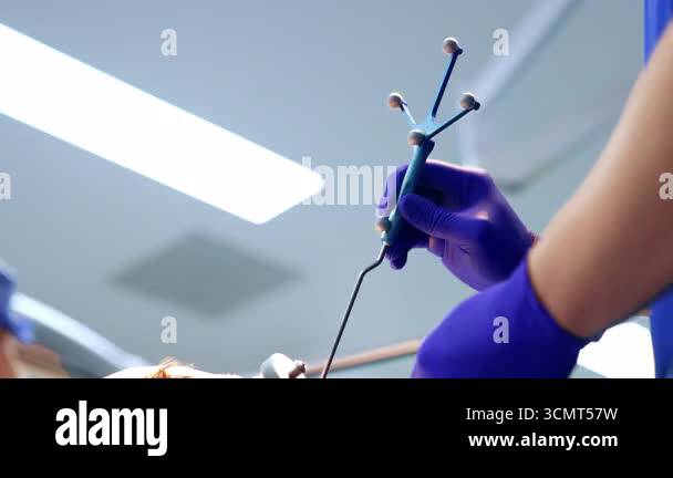 Hands in blue latex gloves holding a neurosurgical probe at the head of ...