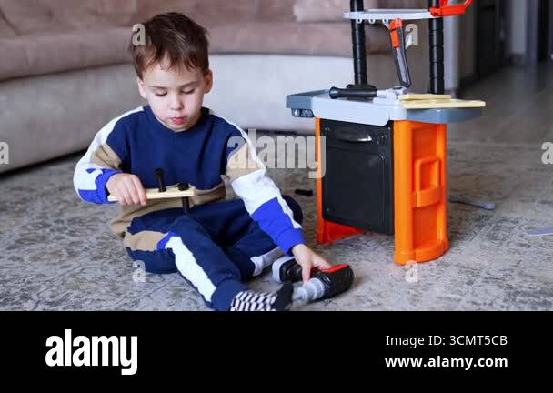 Child plays with toy tools inside. A boy plays on the floor with a toy ...