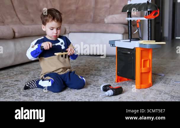 Boy playing with toy tools on the floor. A young boy engages in a ...