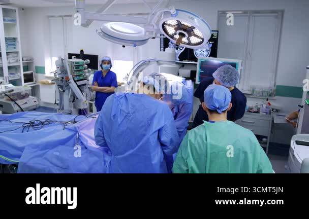 Rear view of male doctors wearing robes stand at the operating table ...