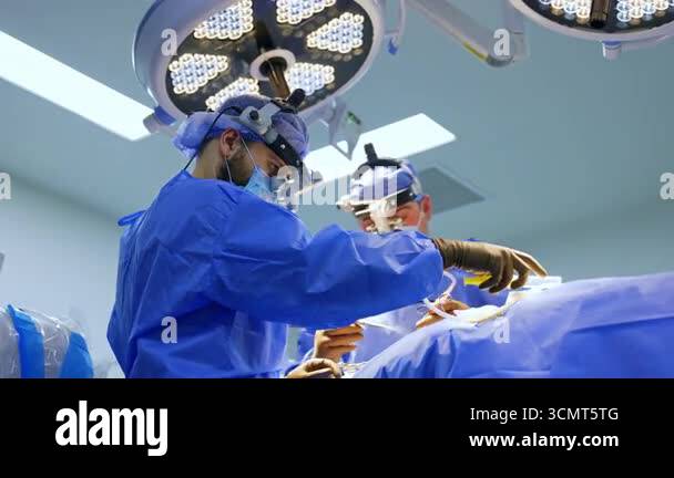 Two professional surgeons equipped with surgical loupes stand at the ...