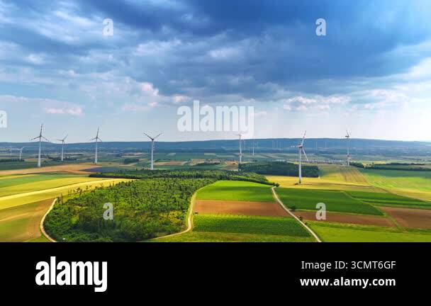 Turbines produce energy in fields. Wind turbines stand tall against a dramatic sky, harnessing ...