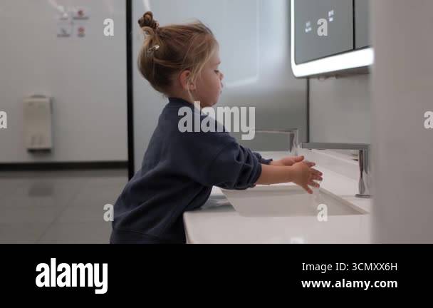Child begins handwashing at modern sink, rubbing soap into rich lather ...