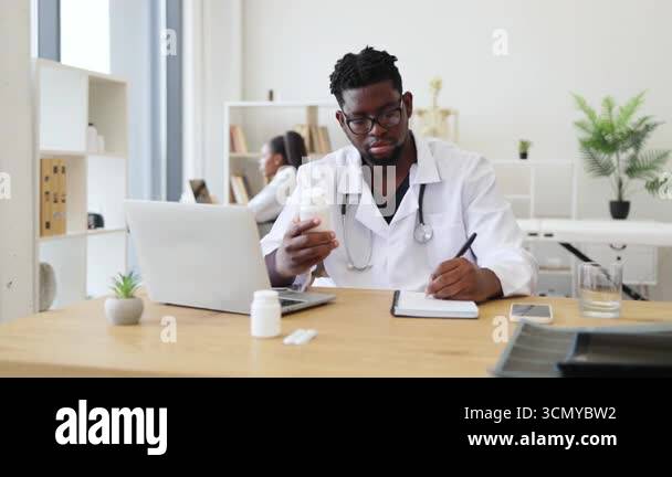 Male doctor sitting at desk in medical office, holding medication ...