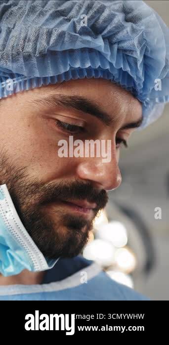 A close-up portrait captures a male surgeon, wearing a surgical cap and ...