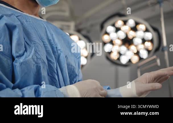 A doctor or surgeon, wearing a mask and surgical gown, stands in an ...