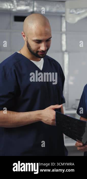Vertical video of a bald doctor wearing scrubs looking at a laptop ...